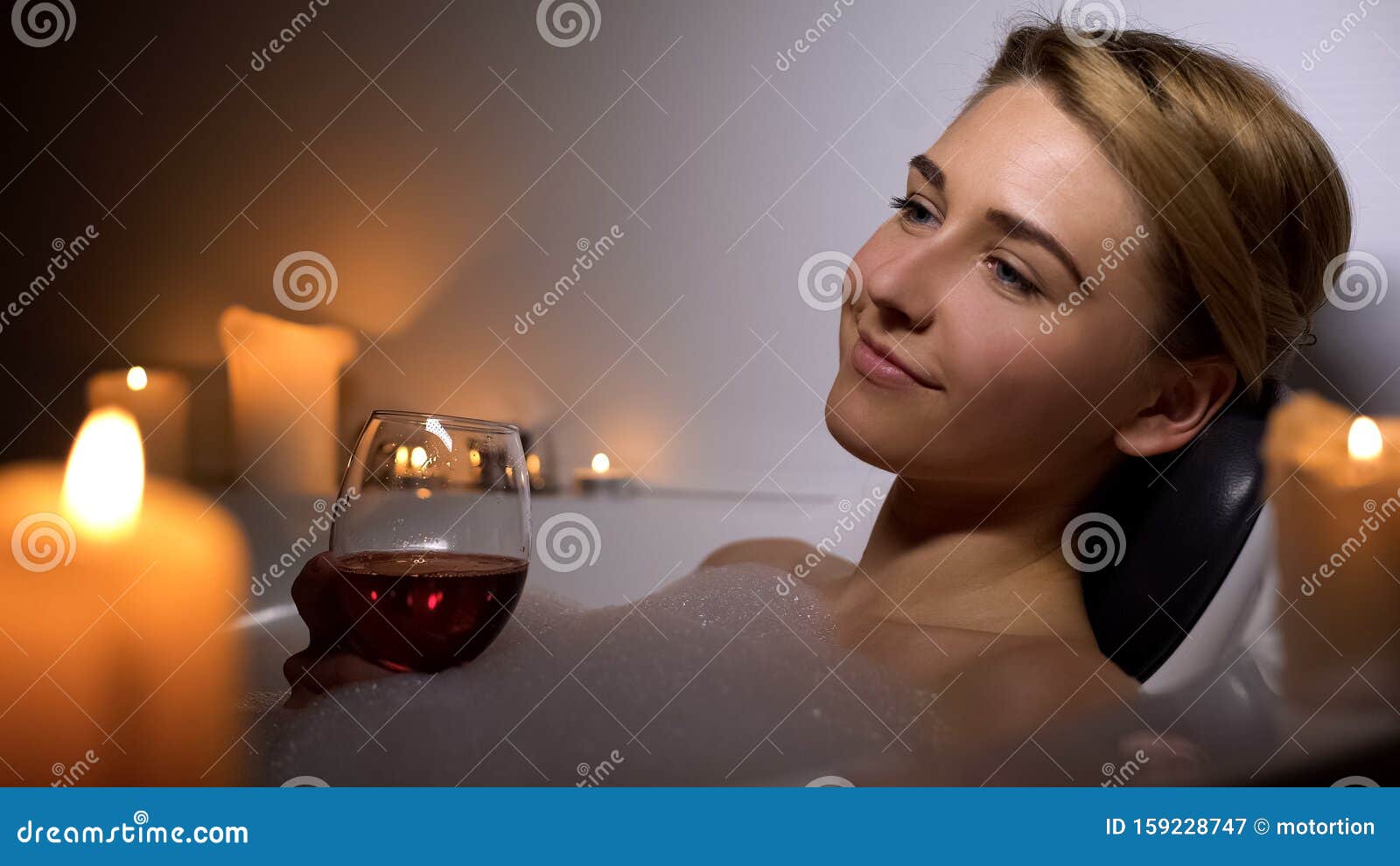 Attractive Woman Lying In Bath With Foam Bubbles And Candles Drinking