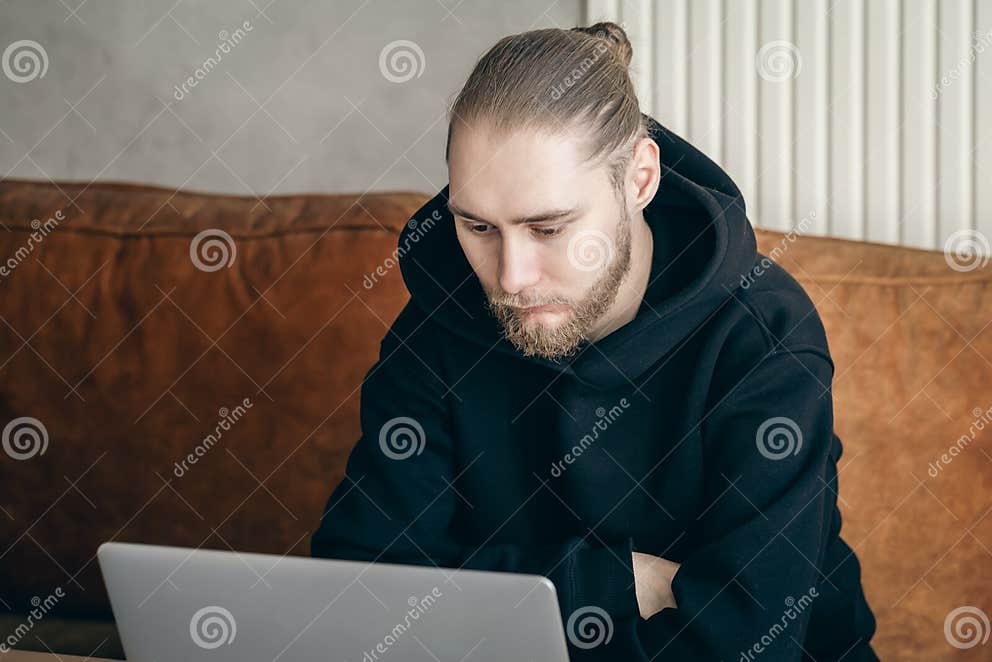 An Attractive Young Man with a Beard is Working on a Laptop. Stock ...