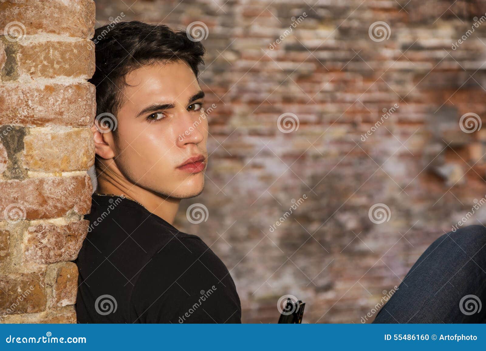 Attractive Young Man Sitting Against Brick Wall Stock Photo - Image of ...