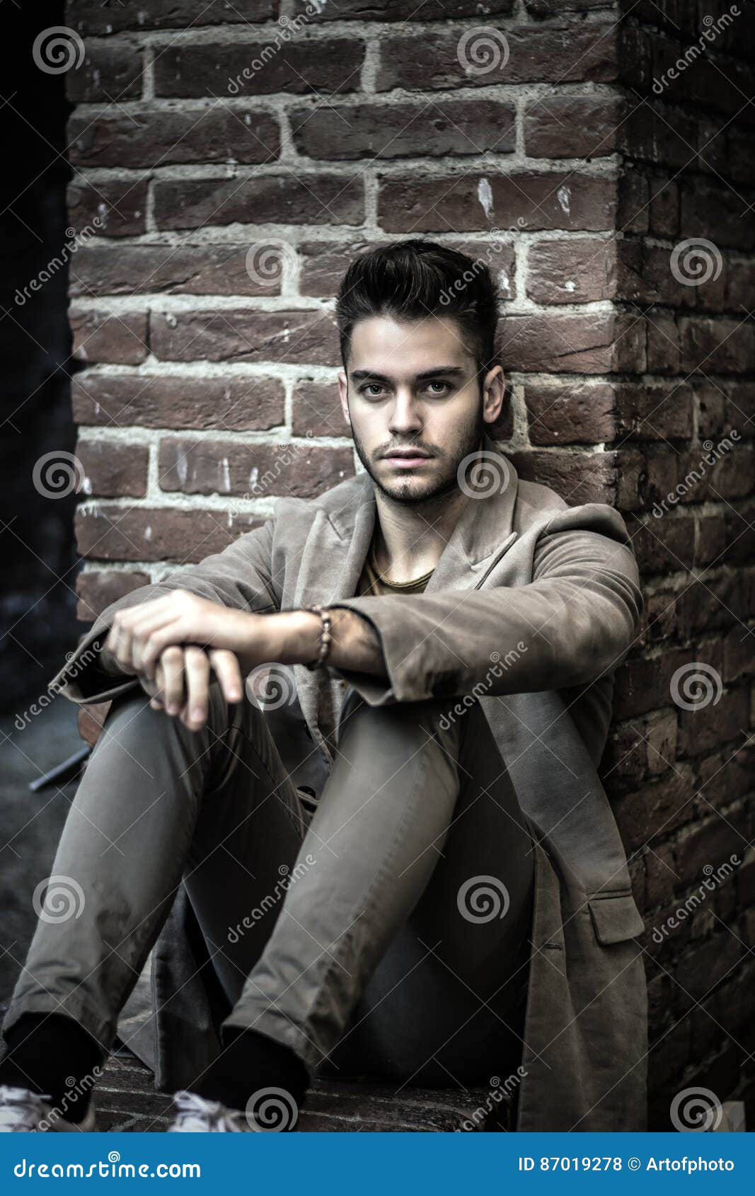 Attractive Young Man Sitting Against Brick Wall Stock Photo - Image of ...