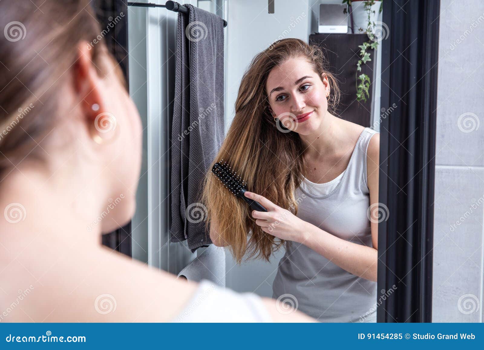 Attractive Young Woman Brushing Long Hair In Front Of Mirror Stock