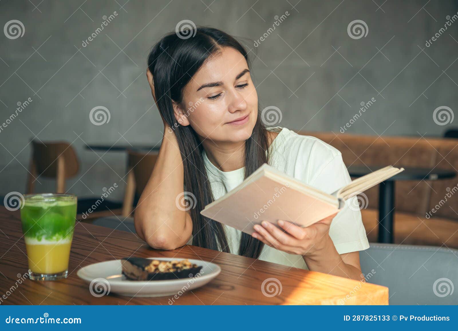 Attractive Young Woman Is Reading A Book While Sitting In A Cafe Stock