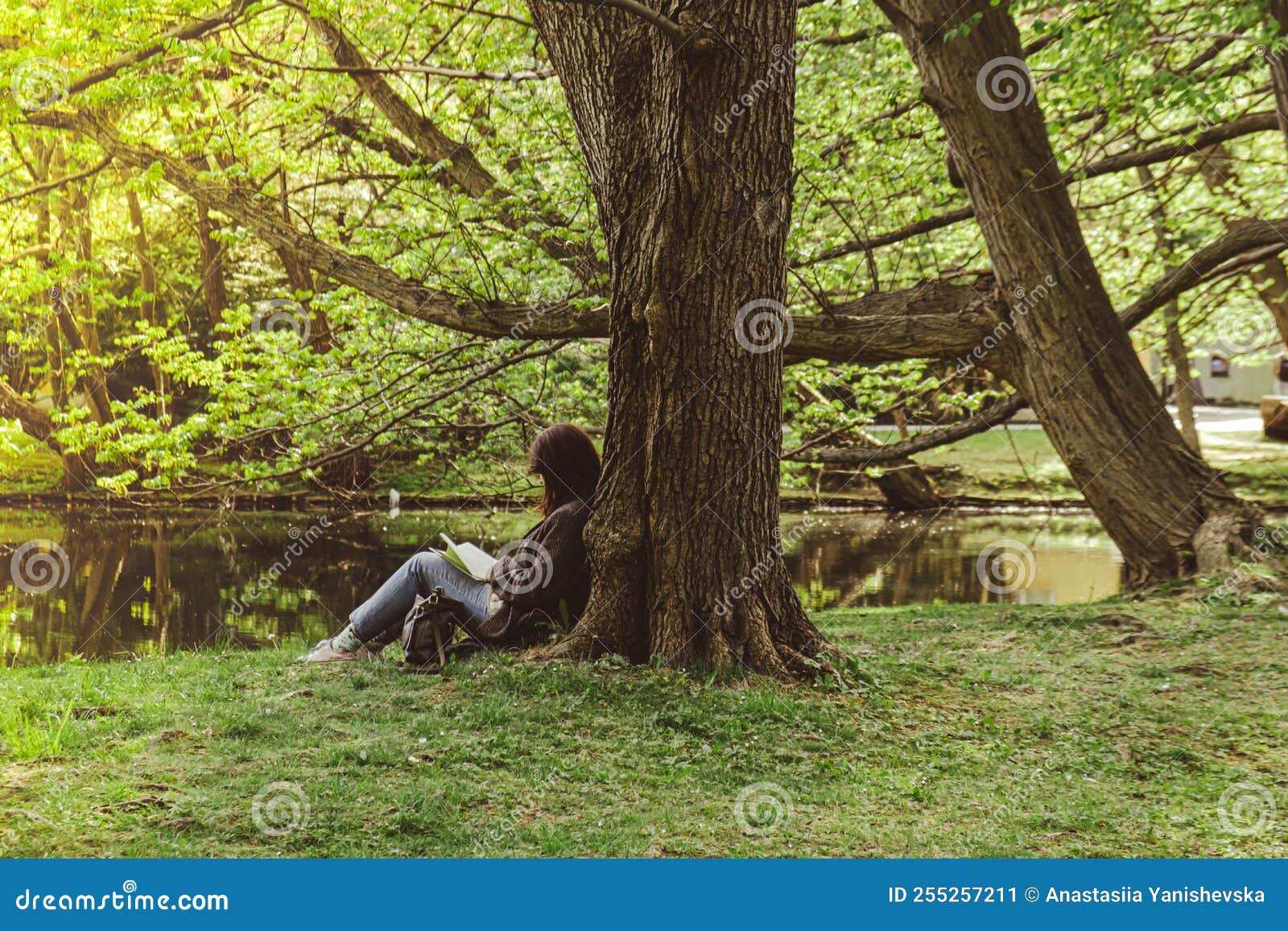 Attractive Young Woman Reading Book While Sitting On Grass In Green