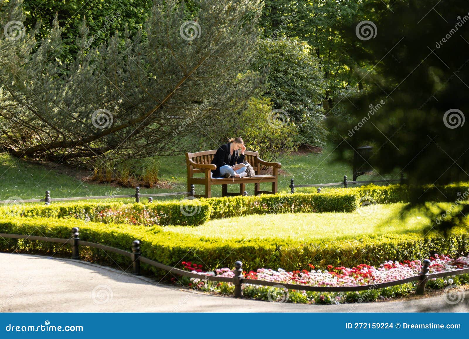 Attractive Young Woman Reading Book While Sitting On Grass In Green