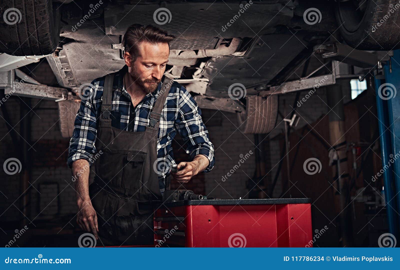 Auto Mechanic in a Uniform, Working on a Workbench while Standing Under ...