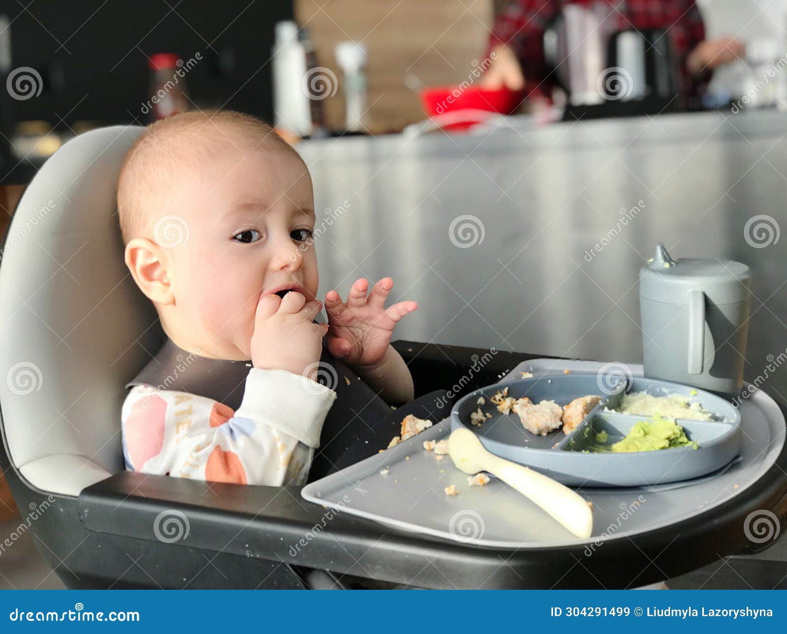 The Baby Eats Independently with His Hands while Sitting at the Feeding ...