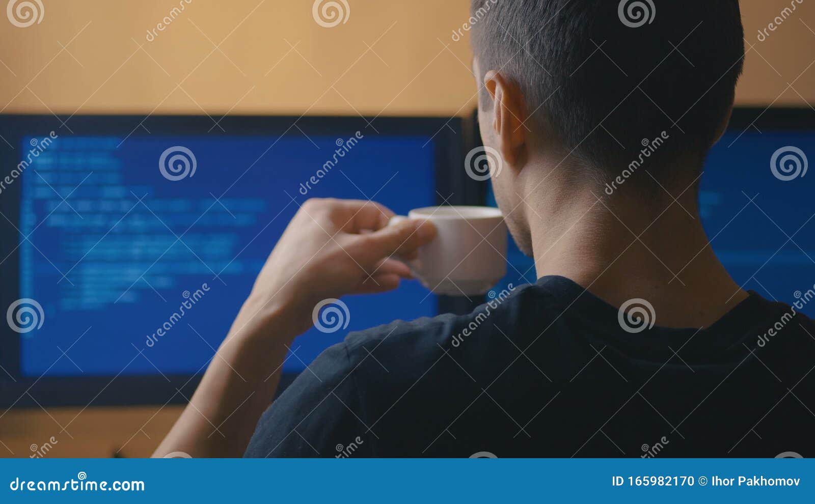 Back View Of Man Programmer Hacker Working And Drinking Coffee At Computer In The Data Center