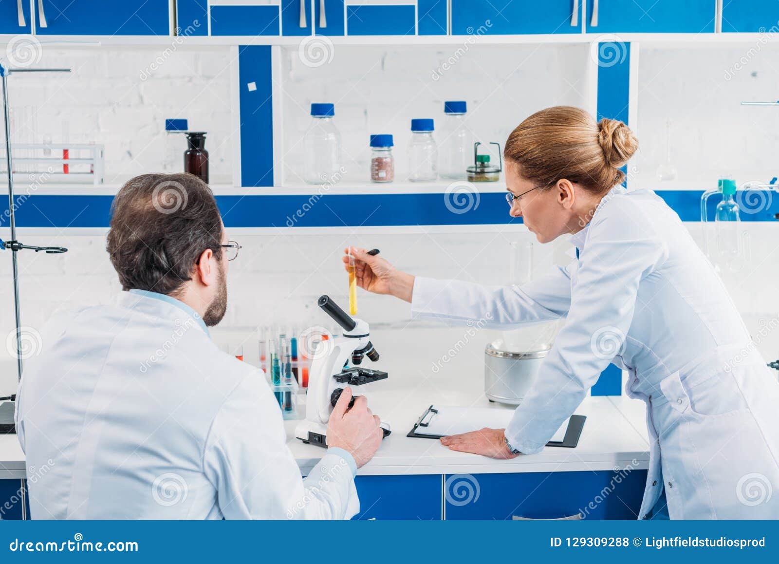 Back View of Scientists in White Coats Looking at Tube with Reagent ...