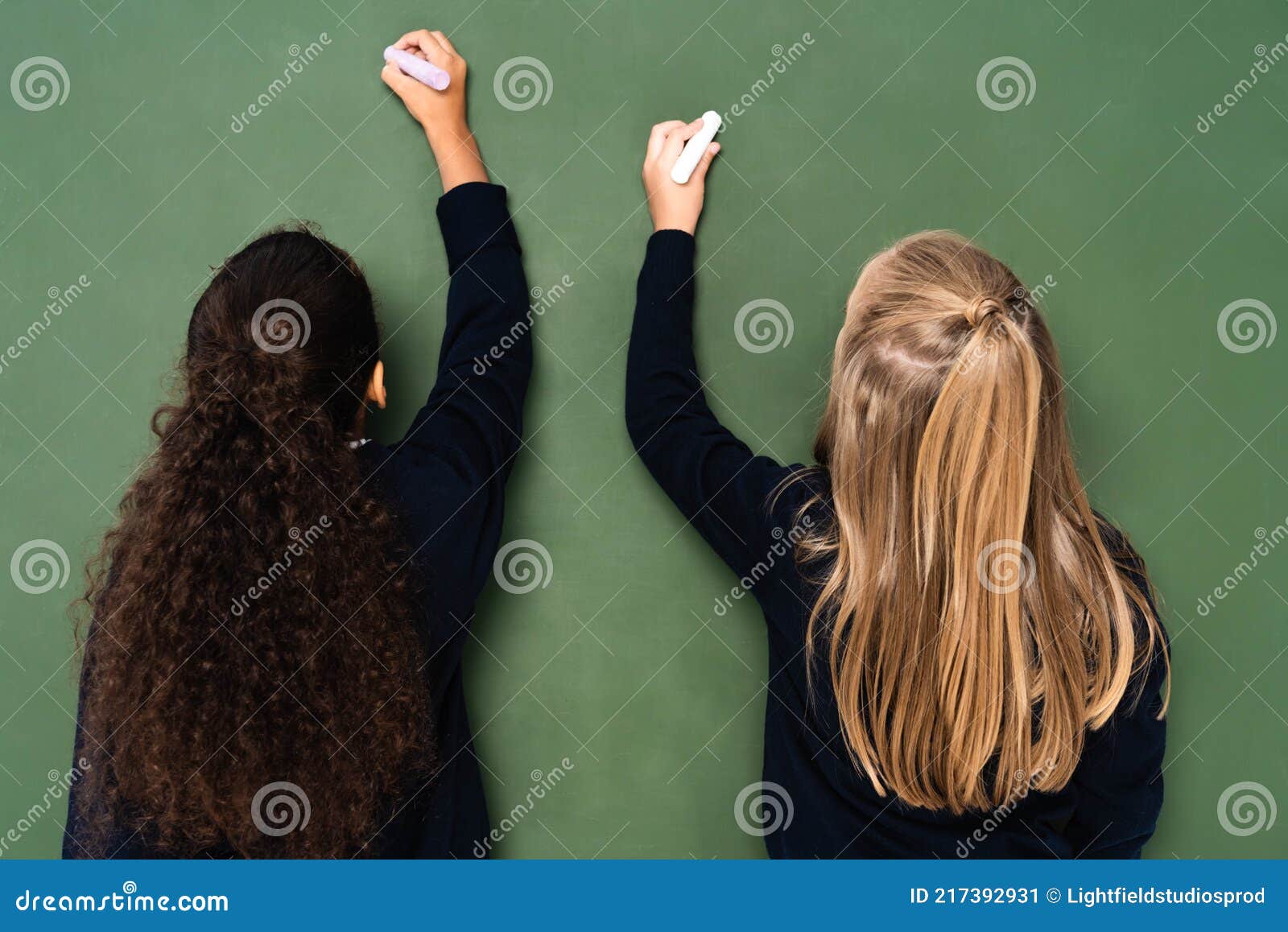 Back View of Two Multicultural Schoolgirls Writing on Chalkboard with ...