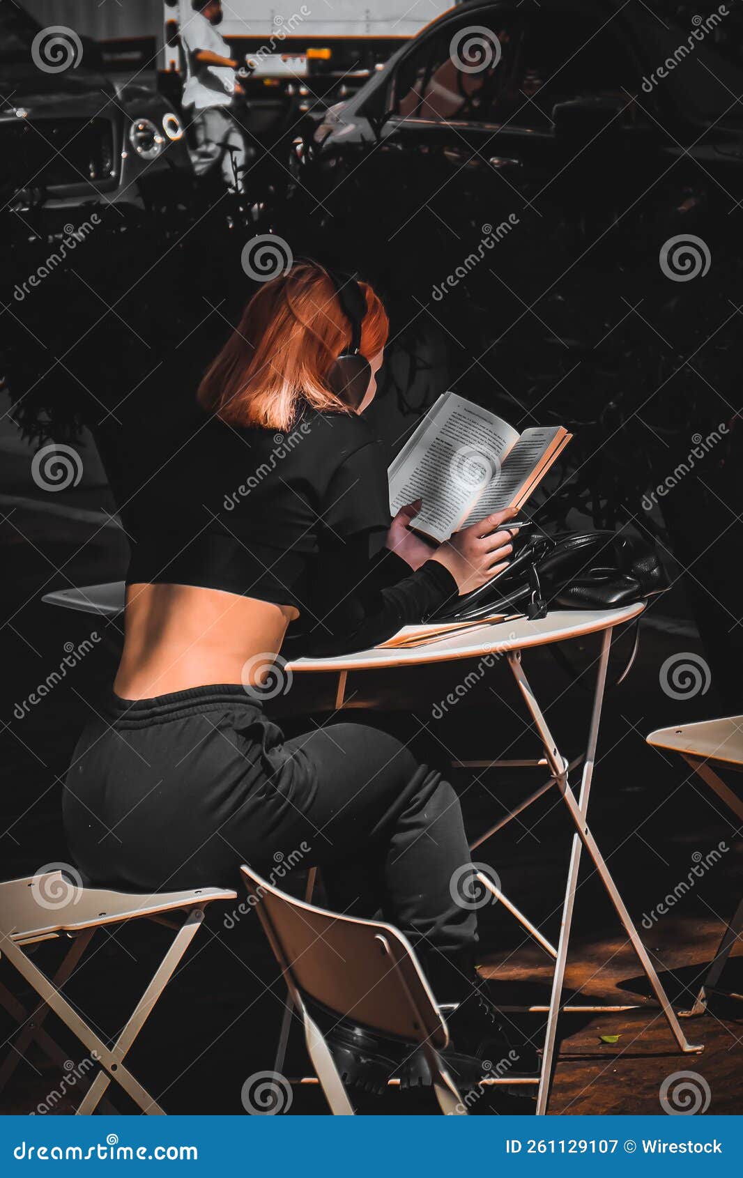 Back View of a Woman Sitting and Reading a Book while Wearing a Headset ...