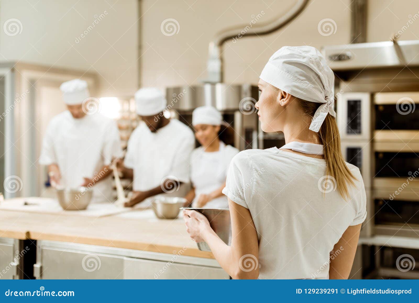 Back View of Young Female Baker at Workplace with Blurred Colleagues ...