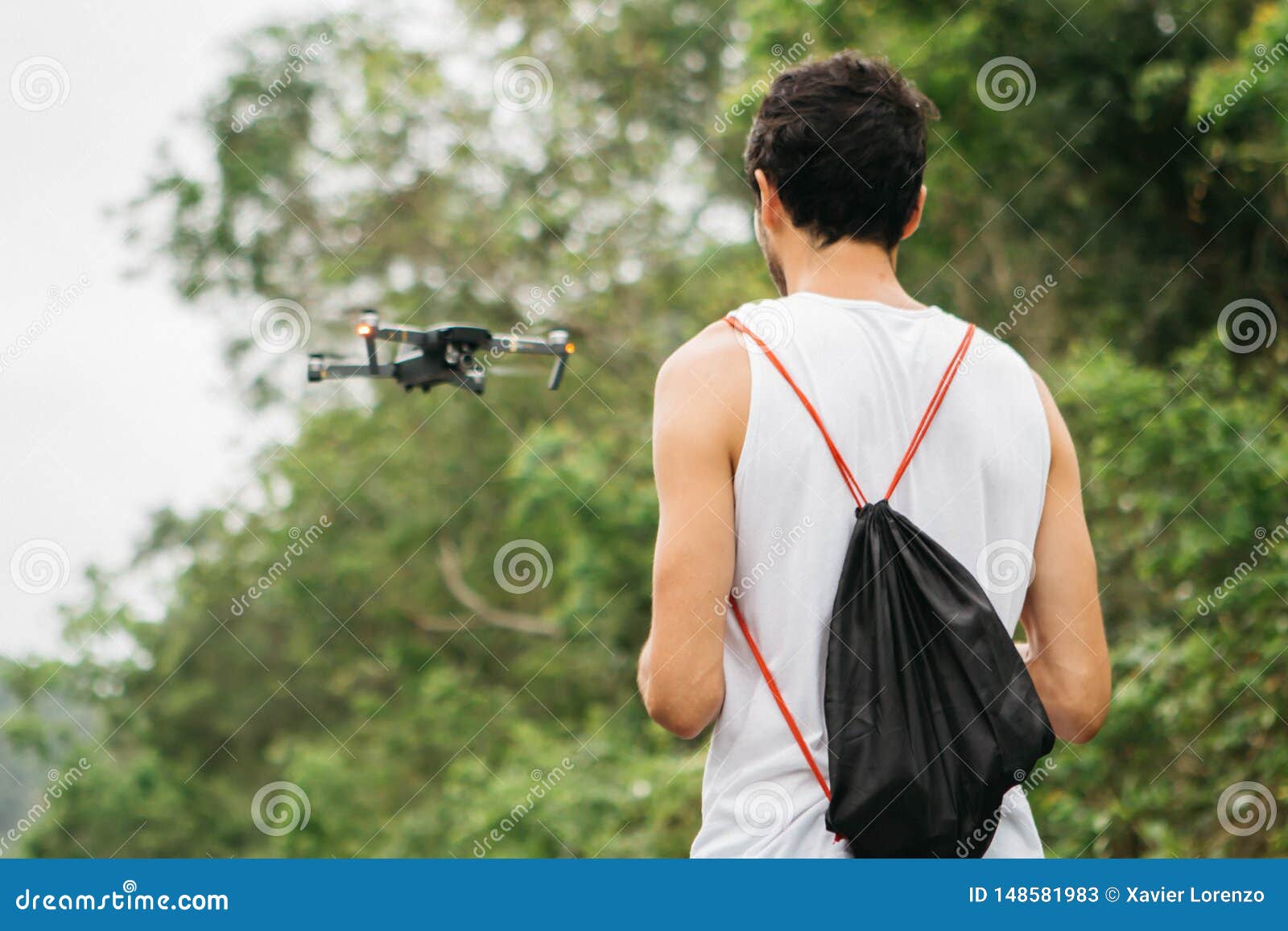 Back View of a Young Man Operating a Drone by Remote Control in the ...