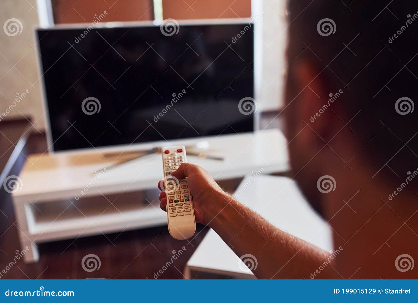 Backing View of Man Holds Remote Controller in Hand and Turning on TV ...