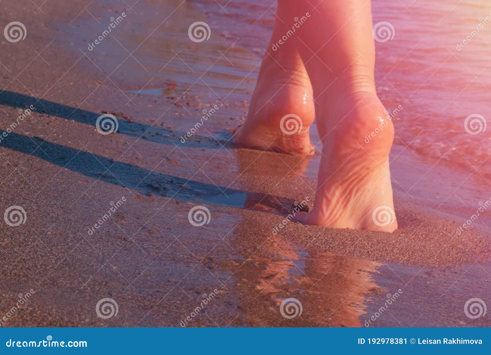 Barefoot Woman Legs Are Walking Along Seaside On Sandy Beach At Rising