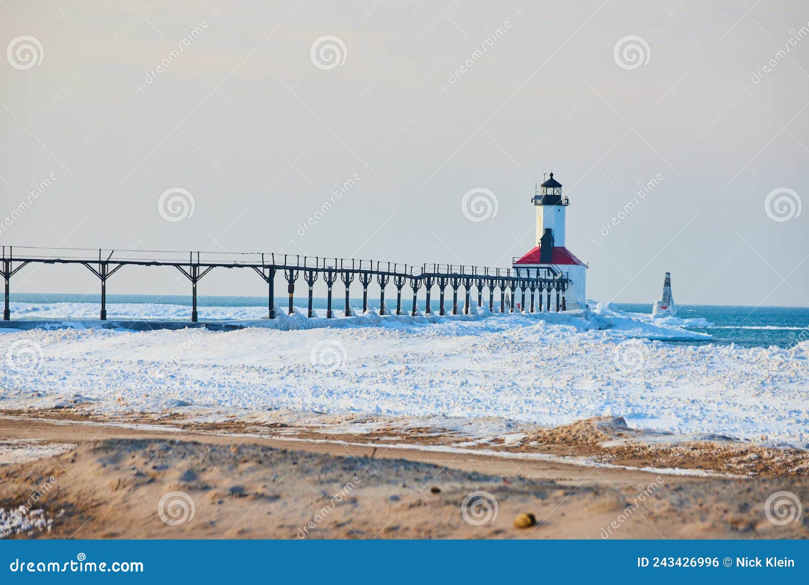 Beach Covered in Ice with Walkway Leading To Red and White Lighthouse ...