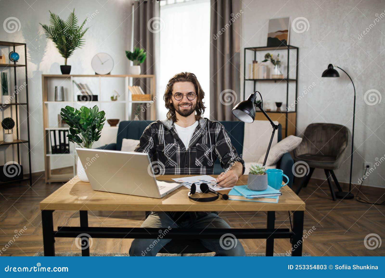 Bearded Young Man In Checkered Shirt And Eyeglasses Sitting At Table