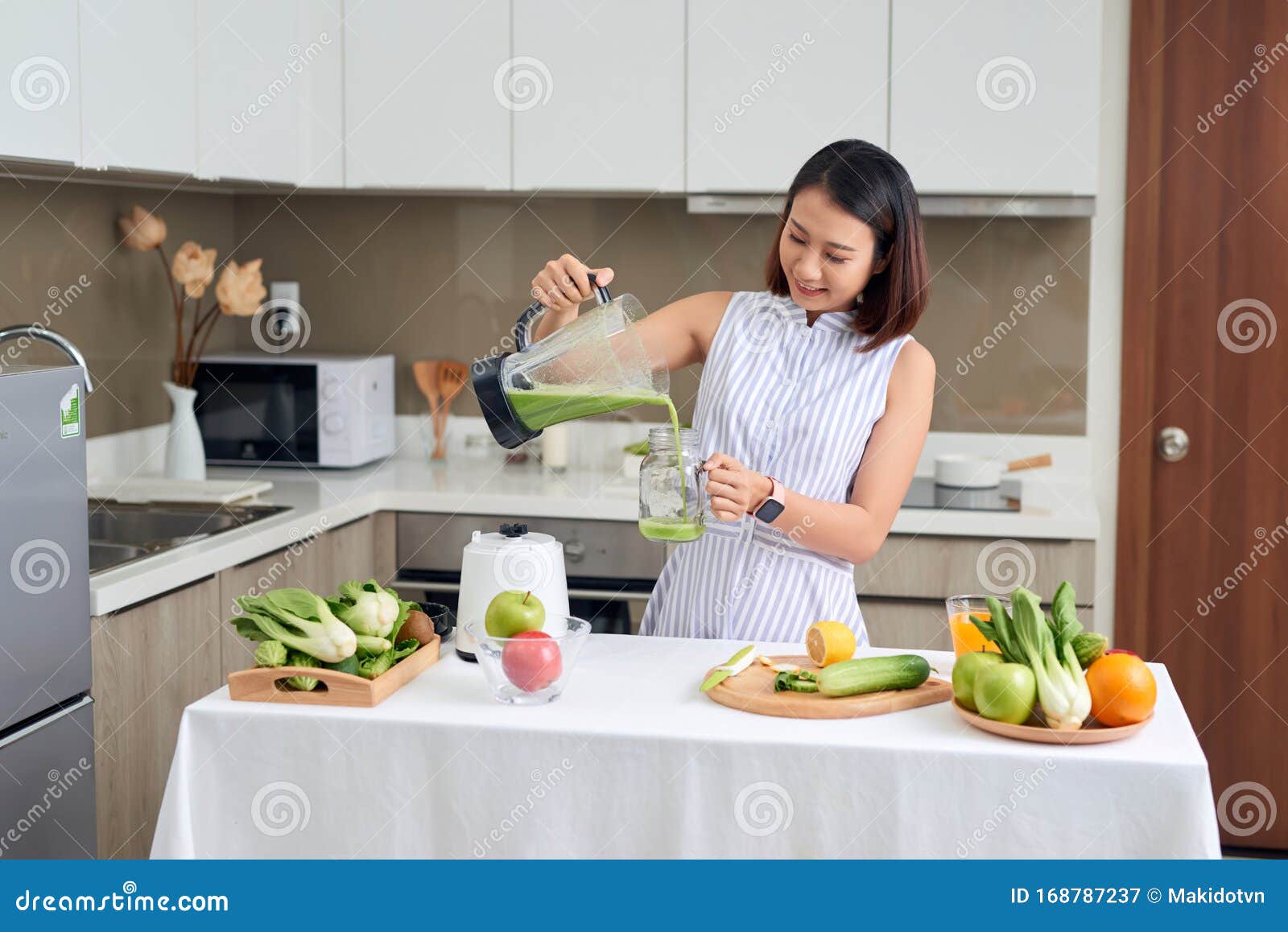 Beautiful Asian Woman Pouring Smoothie From Blender In The Kitchen
