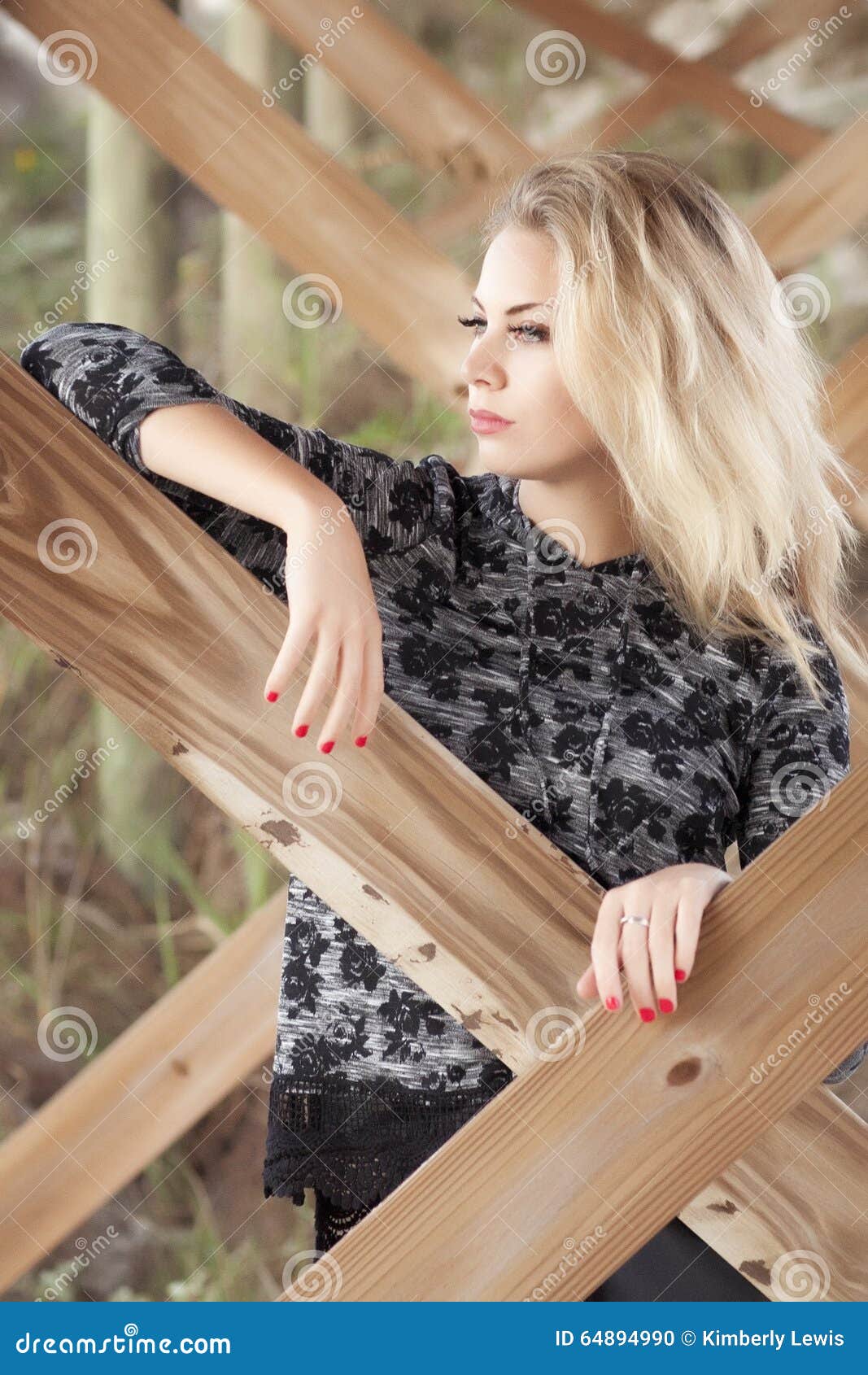A Beautiful Blond Woman Standing Under A Pier By The Ocean Looking Away