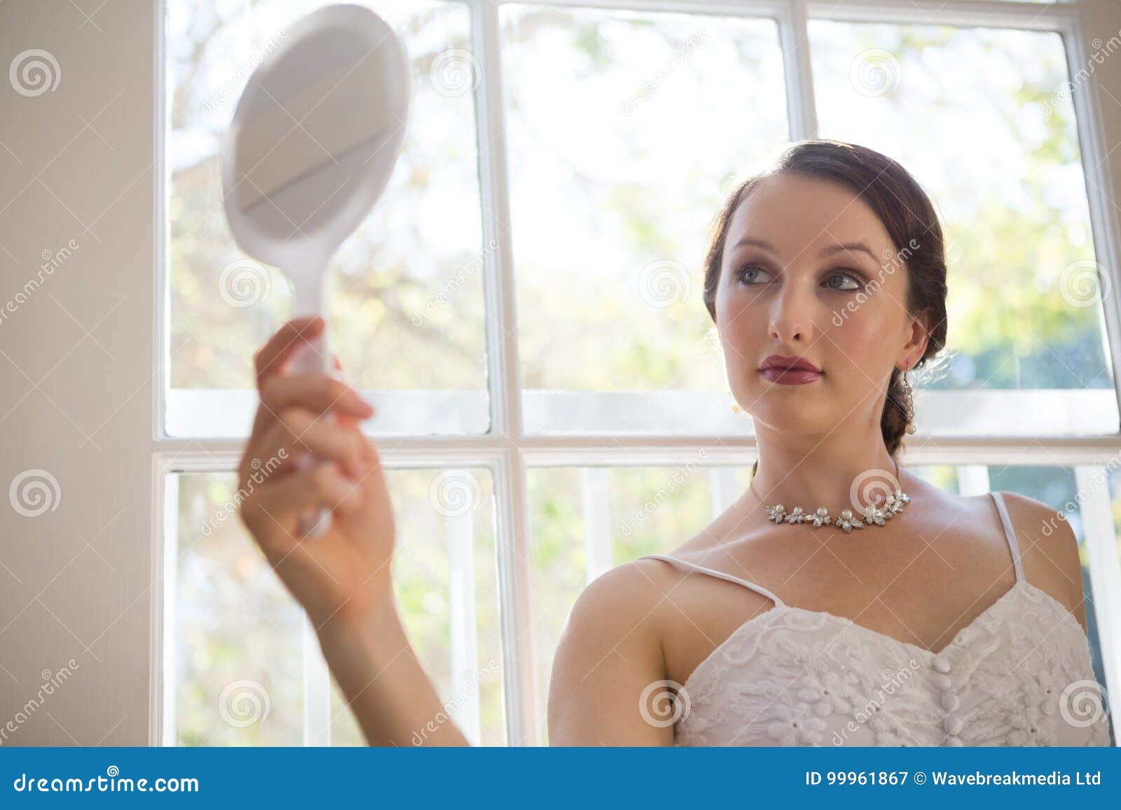 Beautiful Bride Looking into Hand Mirror while Standing by Window at ...