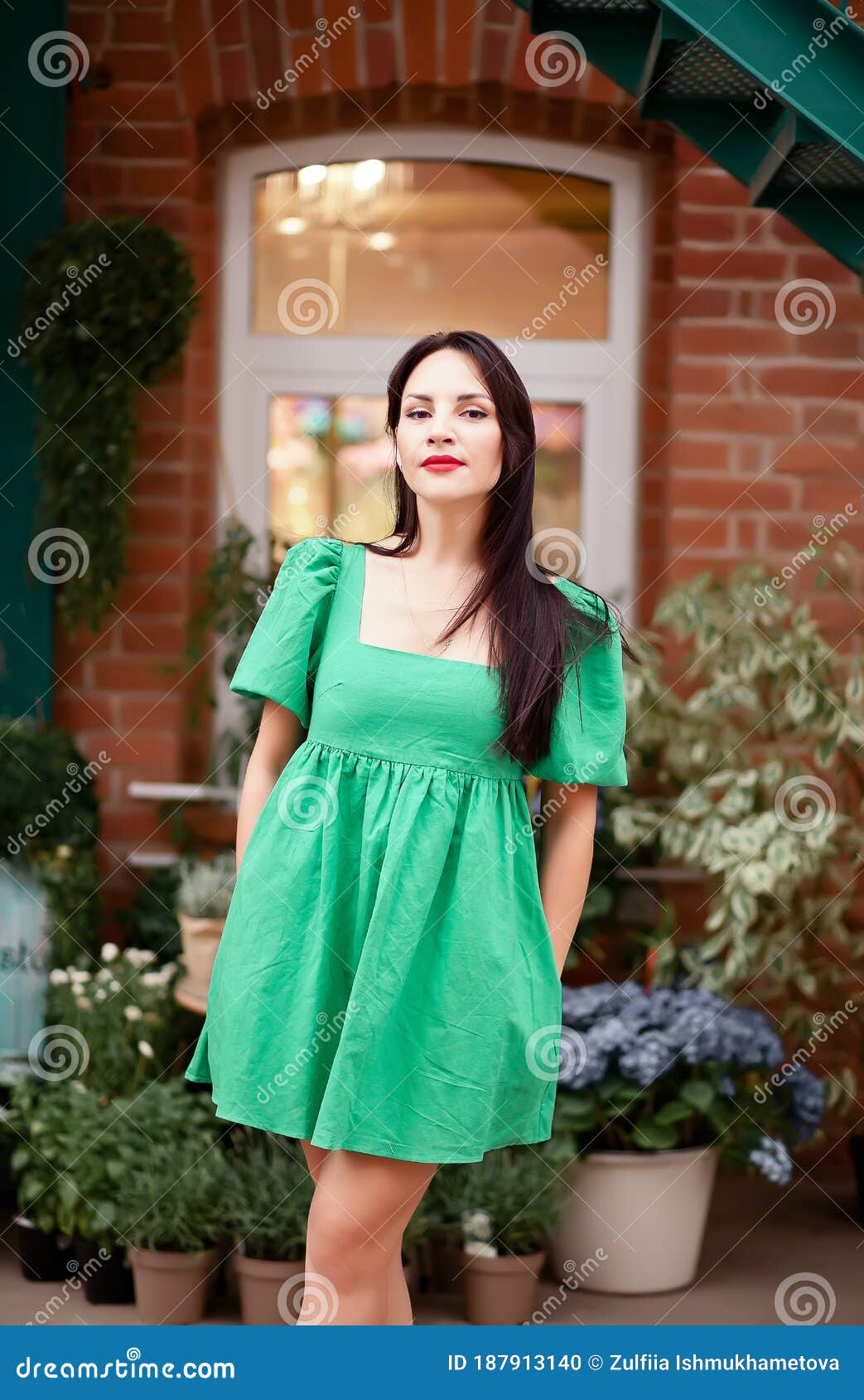 Beautiful Brunette Woman In A Green Dress Standing Near A Flowers Store