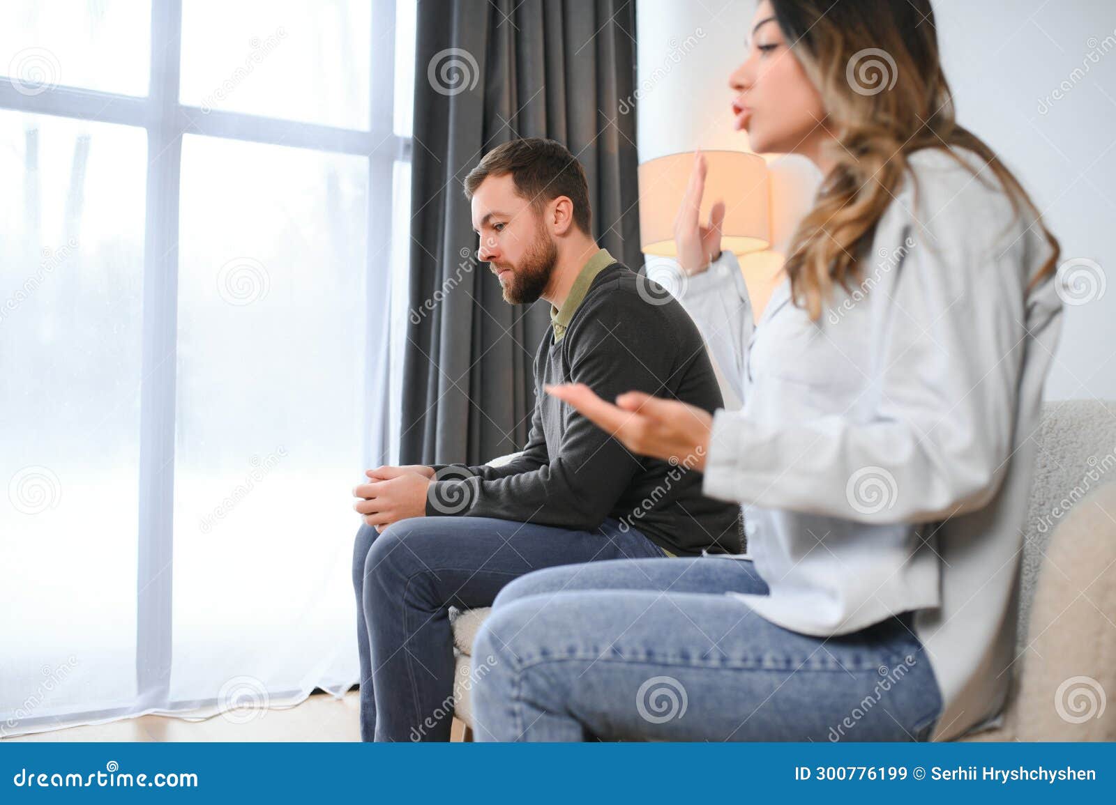Beautiful Couple Is Sitting Back To Back On The Couch While Having A