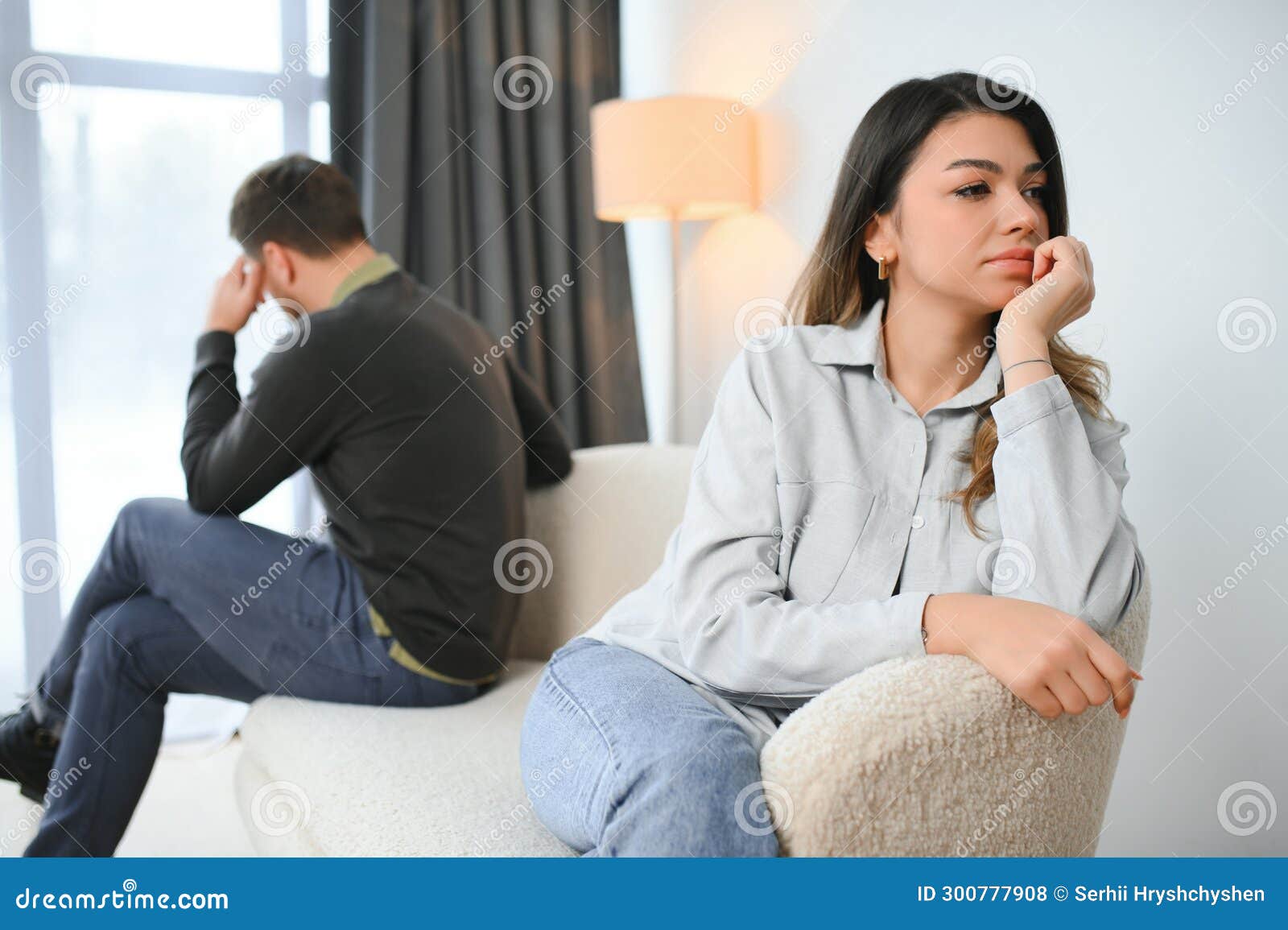 Beautiful Couple Is Sitting Back To Back On The Couch While Having A