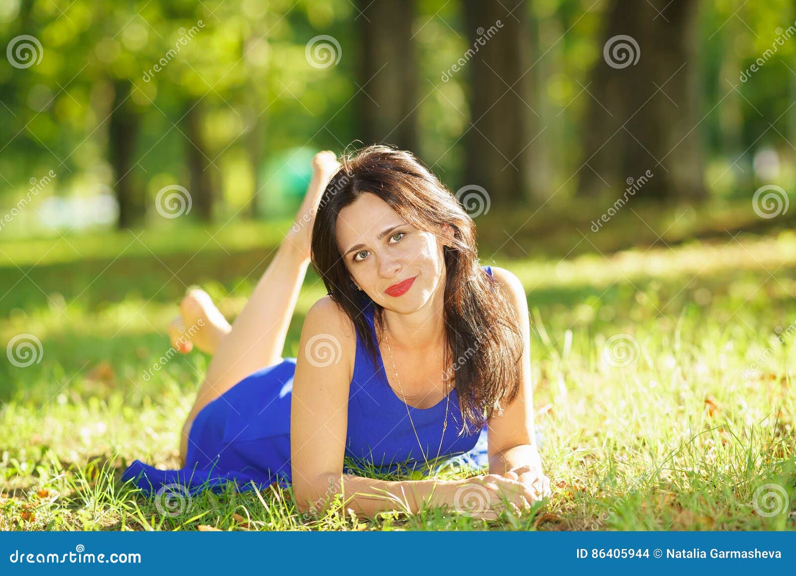 Beautiful Happy Young Woman In Blue Dress Lying On The Grass Stock