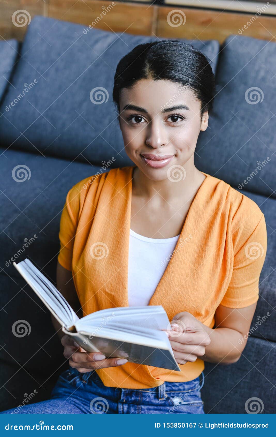Beautiful Mixed Race Girl In Orange Shirt Holding Book In Living Room