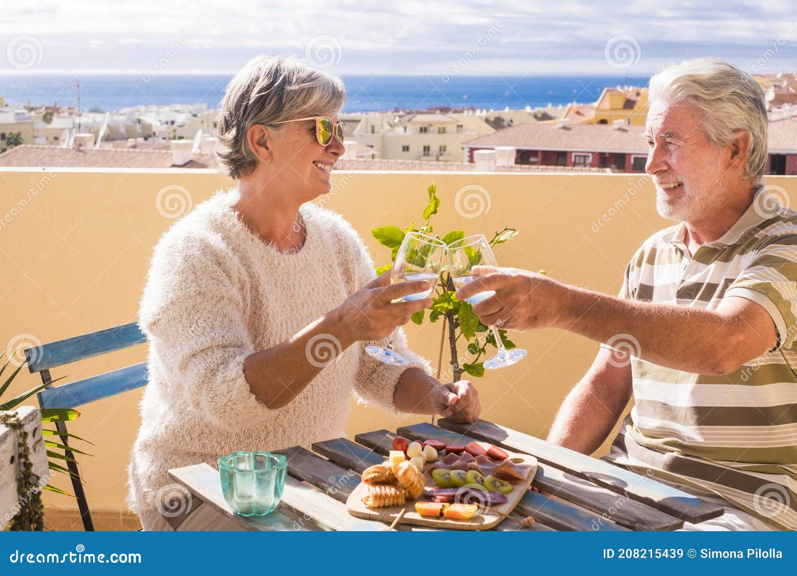 Beautiful Old Mature Couple Enjoy Together Clinking And Roasting Cocktails Outdoor At Home At