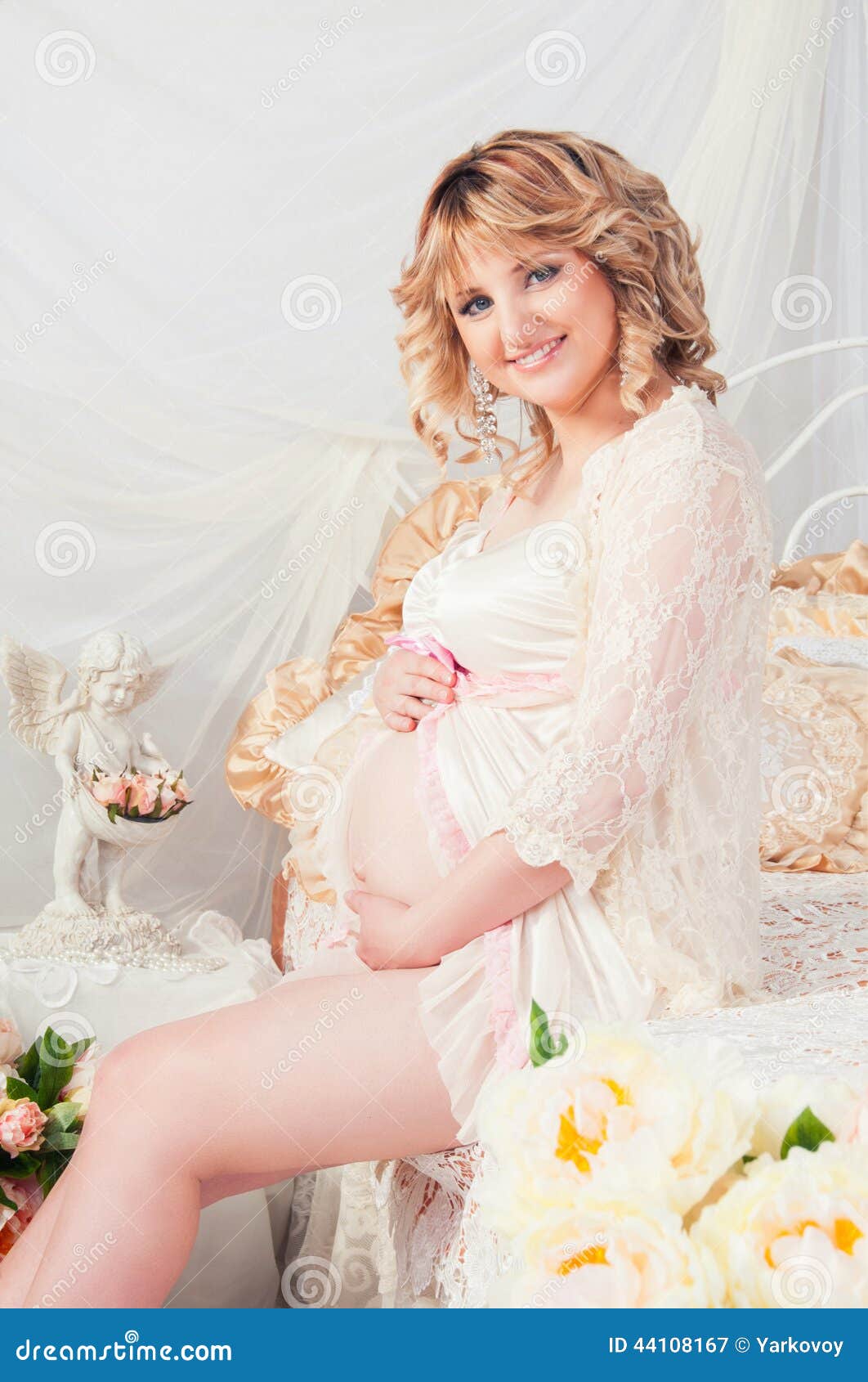 Beautiful Pregnant Woman In A Lace Negligee Sitting On A Bed Of Flowers