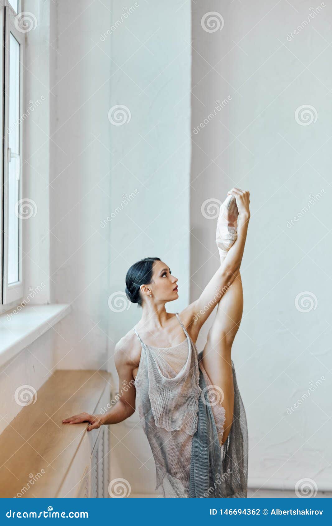 Ballerina In Stage Dress Stretching Leg In Vertical Split Near Window