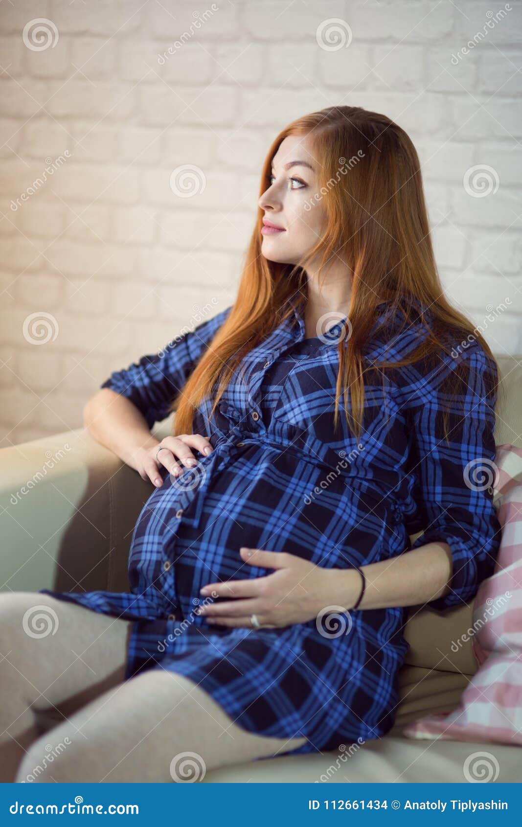 Red Haired Young Pregnant Woman Sitting At Home On The Couch And Stock