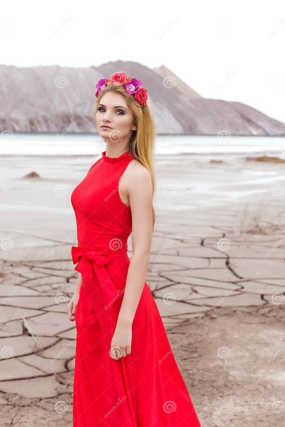 Beautiful Cute Girl With Long Blond Hair In A Long Red Evening Dress With A Wreath Of Roses And