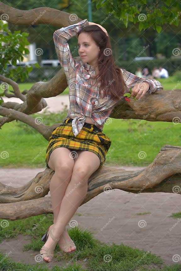 Slender Brunette Girl In A Plaid Skirt And Blouse In The Summer By A
