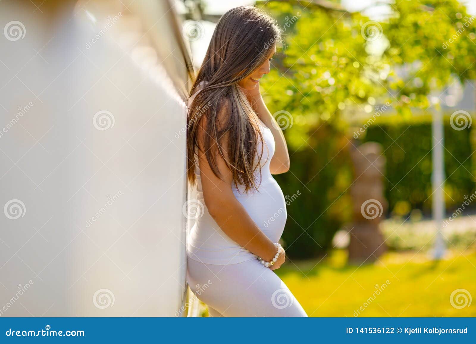 Beautiful Pregnant Woman Standing In Garden Holding Hands On Belly