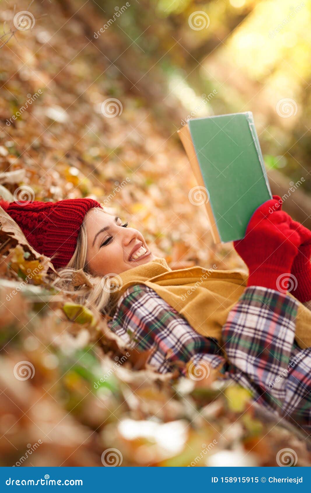 Smiling Young Woman Lying In Autumn Leaves With Book Stock Image