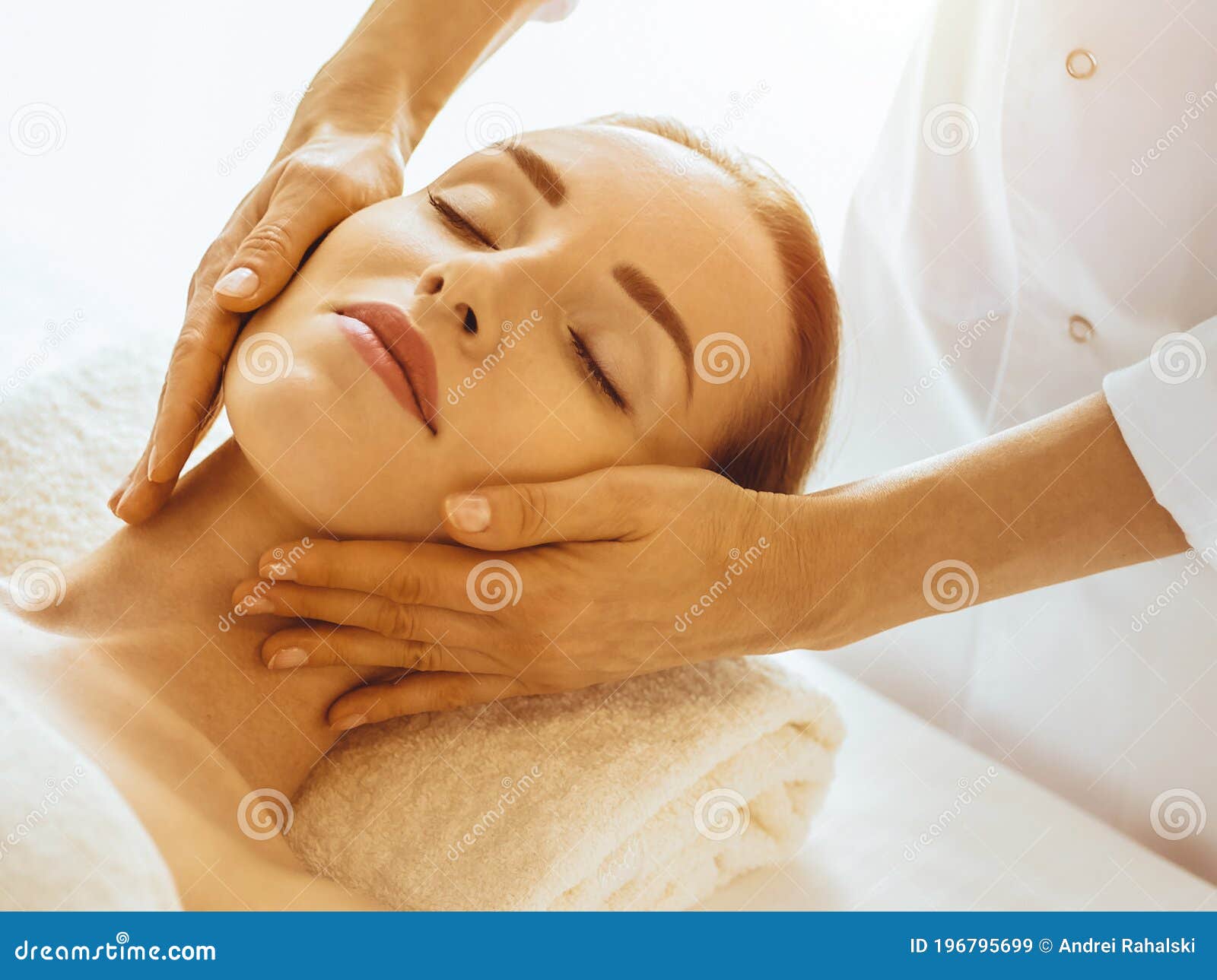 Beautiful Woman Enjoying Facial Massage With Closed Eyes In Sunny Spa