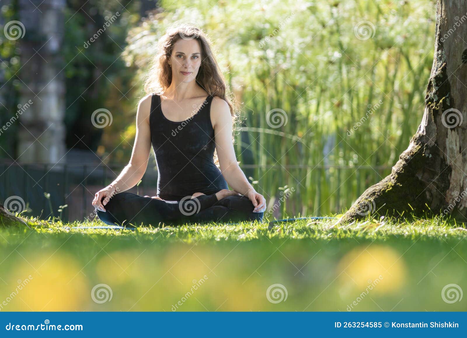 Beautiful Woman Sitting In The Lotus Position On Yoga Mat And Looking