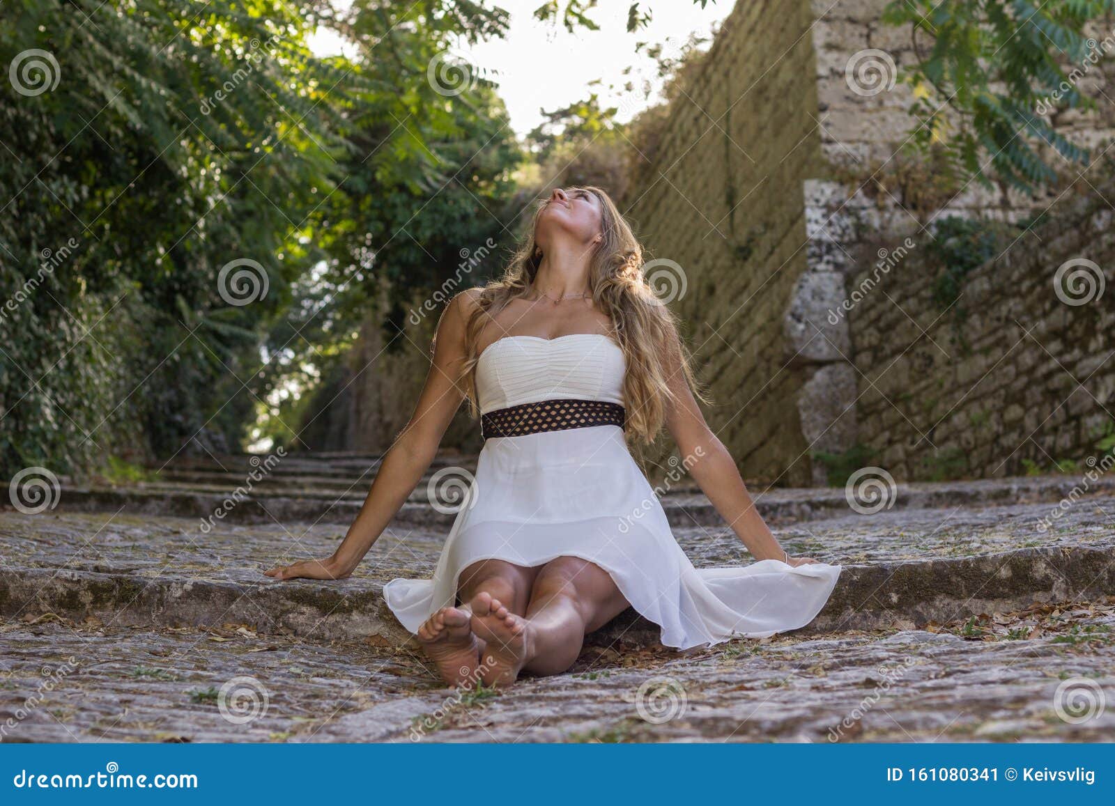 Beautiful Woman Wearing White Dress Sitting On Stone Road Stock Image