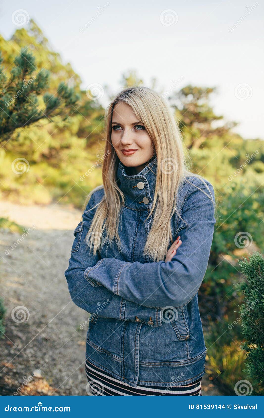 Beautiful Young Blonde Woman In Denim Jacket Standing With Folded Hands