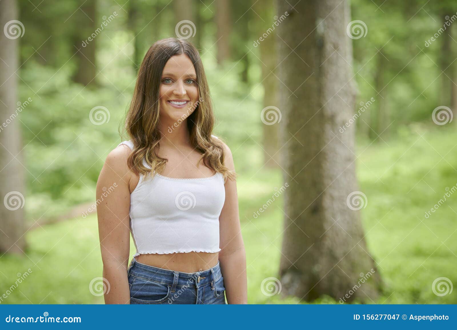 Gorgeous Young Woman In Blue Jeans And White Tank Top Poses Outside