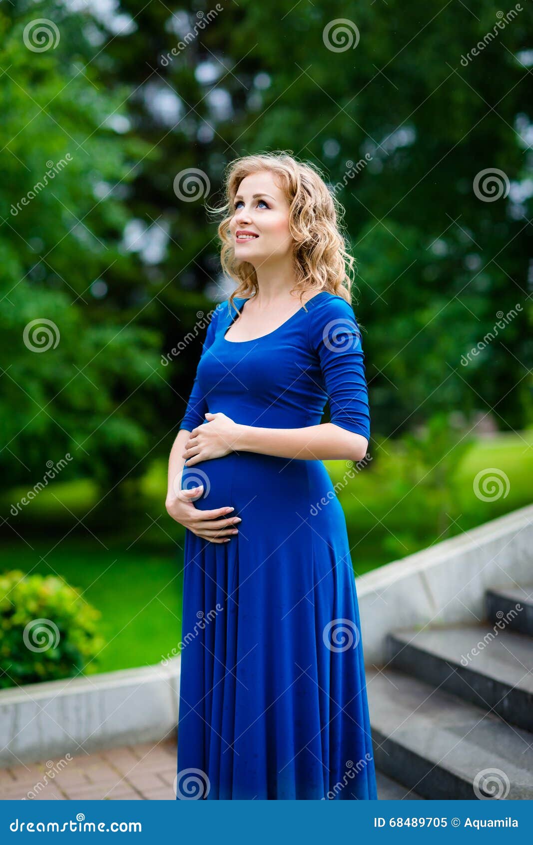Beautiful Young Pregnant Woman In Blue Dress With Long Blond Curly Hair Holding Her Belly