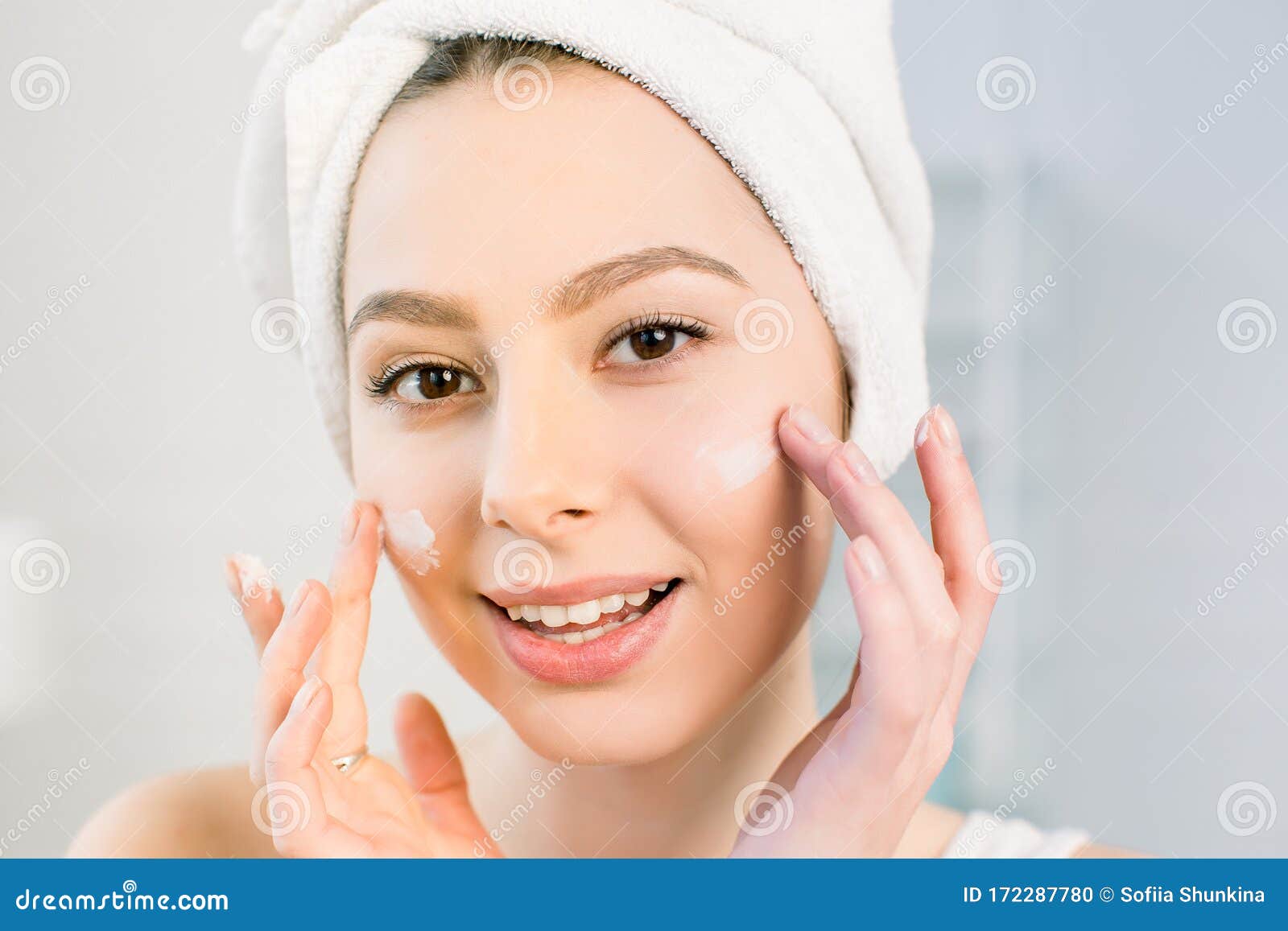 Beautiful Young Woman Applying Cream On Her Face In Bathroom Treatment