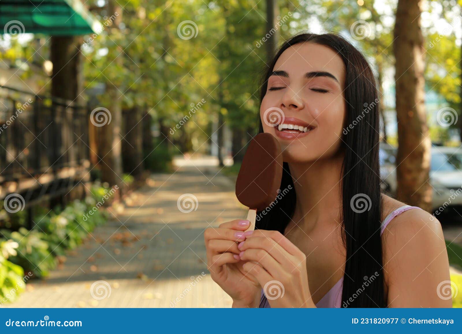 Beautiful Young Woman Eating Ice Cream Glazed In Chocolate On City
