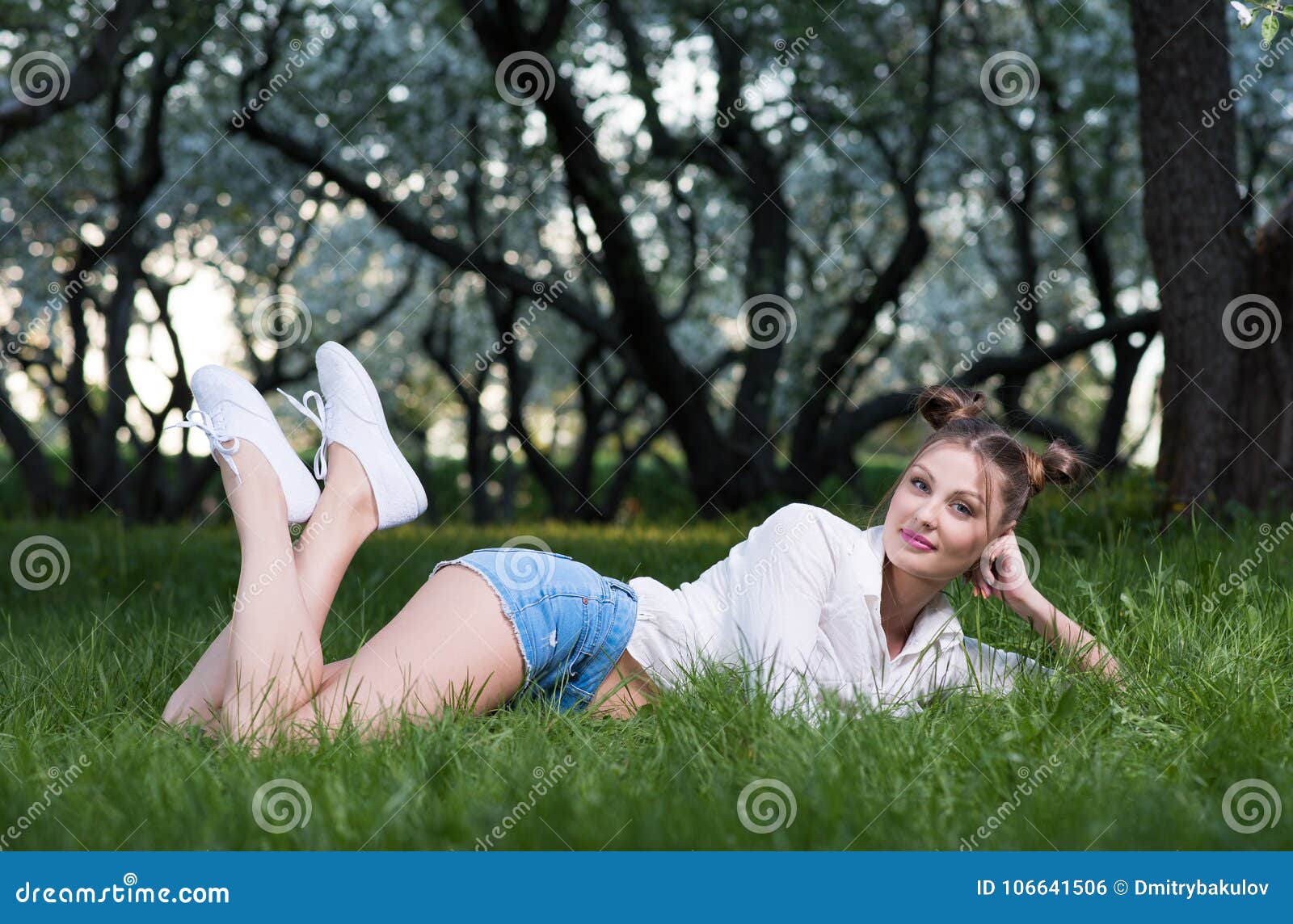 Beautiful Young Woman Lying In The Park On The Grass Lifting Her Legs