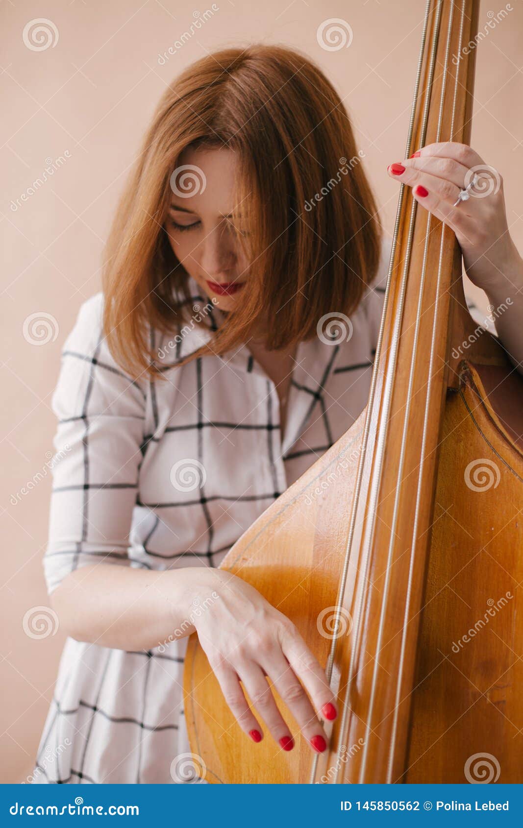 Beautiful Young Woman Musician Sitting On A Vintage Double Bass On A Beige Background Stock