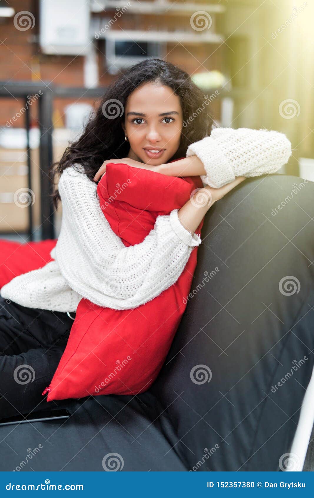 Beautiful Young Woman Sitting On Cosy Sofa At Home Hugging A Pillow