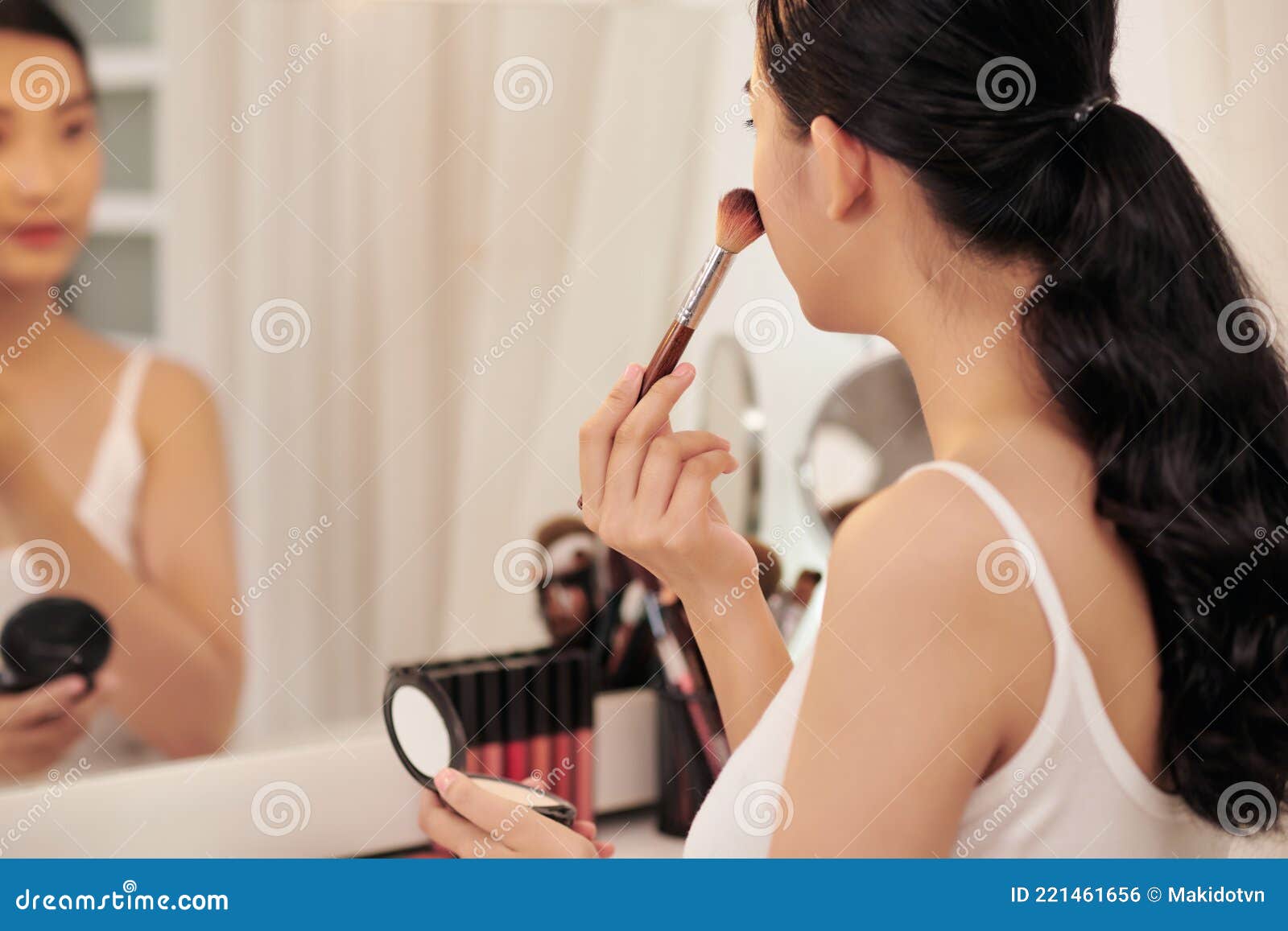 A Beautiful Young Woman Sitting at a Makeup Table and Doing Her Makeup ...