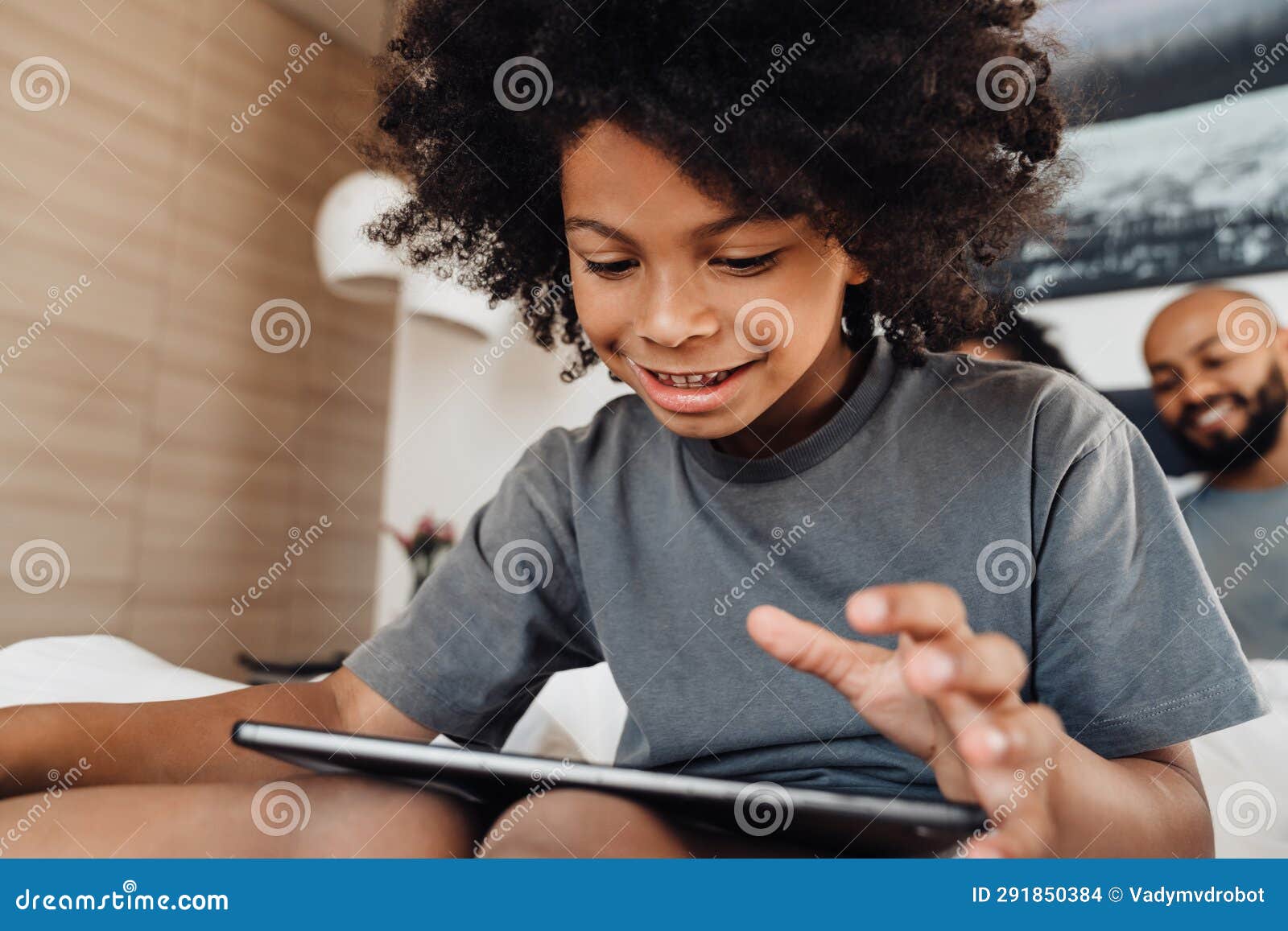 Black Boy Using Tablet Computer while Sitting on Bed with His Family ...