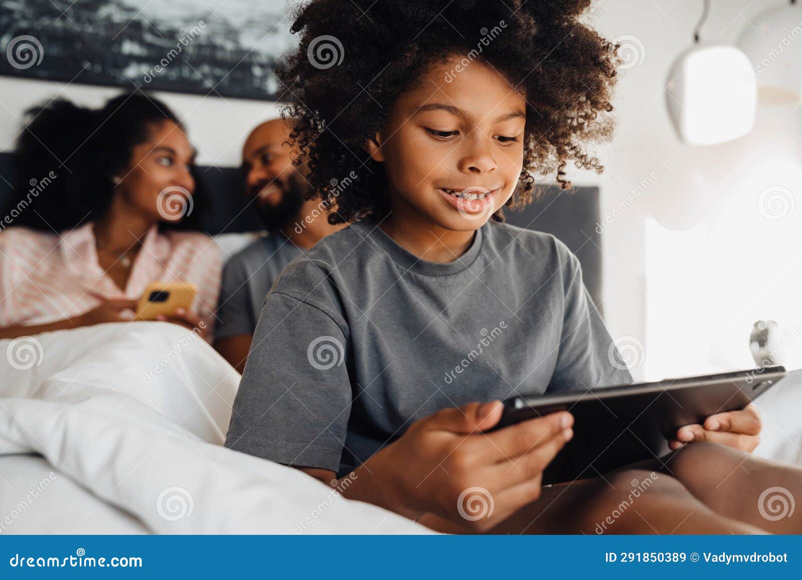 Black Boy Using Tablet Computer while Sitting on Bed with His Family ...